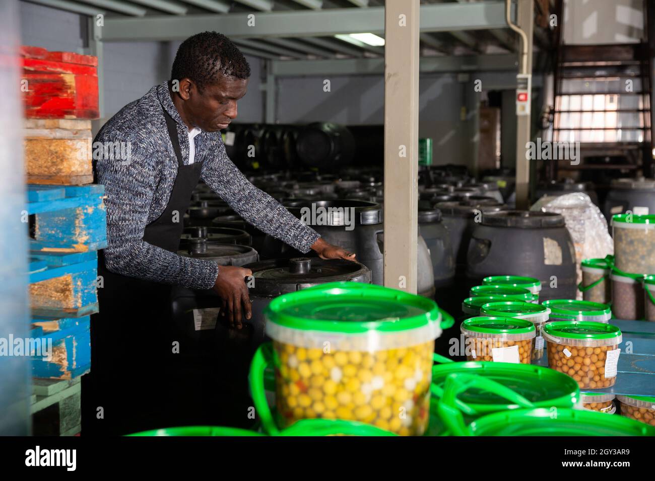 african-american man opens barrel with olives in factory warehouse ...