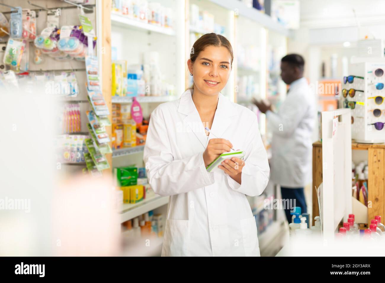 Young smiling female pharmacist making important notes in a notebook ...