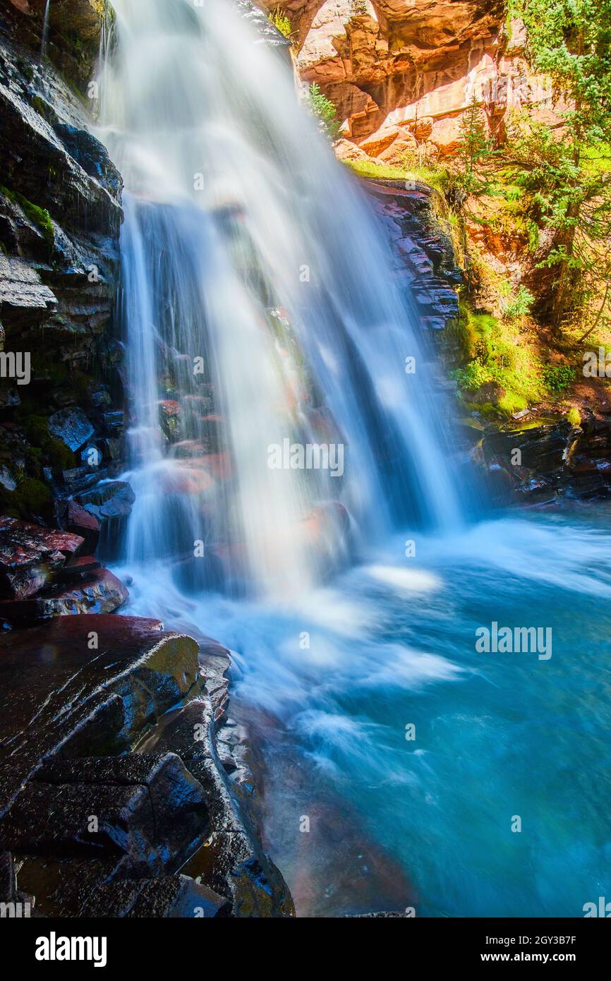 Detail of waterfall over cliffs with red rocks and moss into blue ...