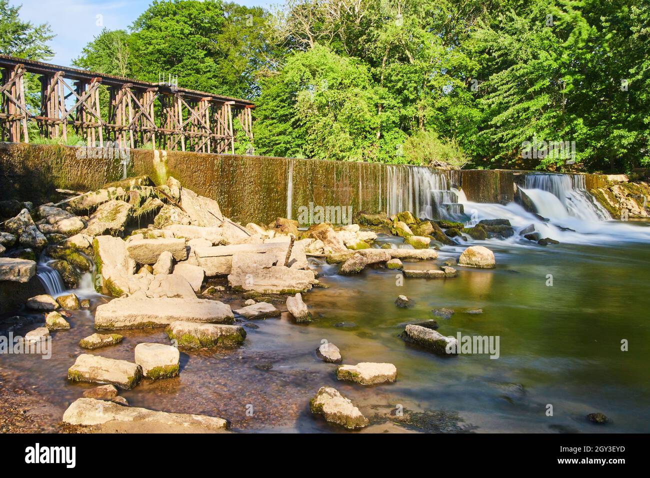 Stone dam creating waterfalls into rocks with railroad bridge in ...