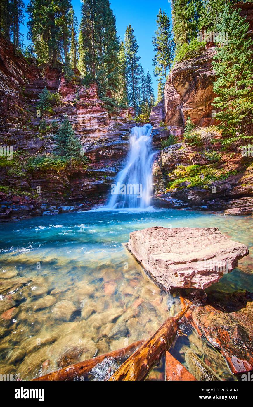 Canyon with waterfall pouring from rocks into bay of sunny blue water ...
