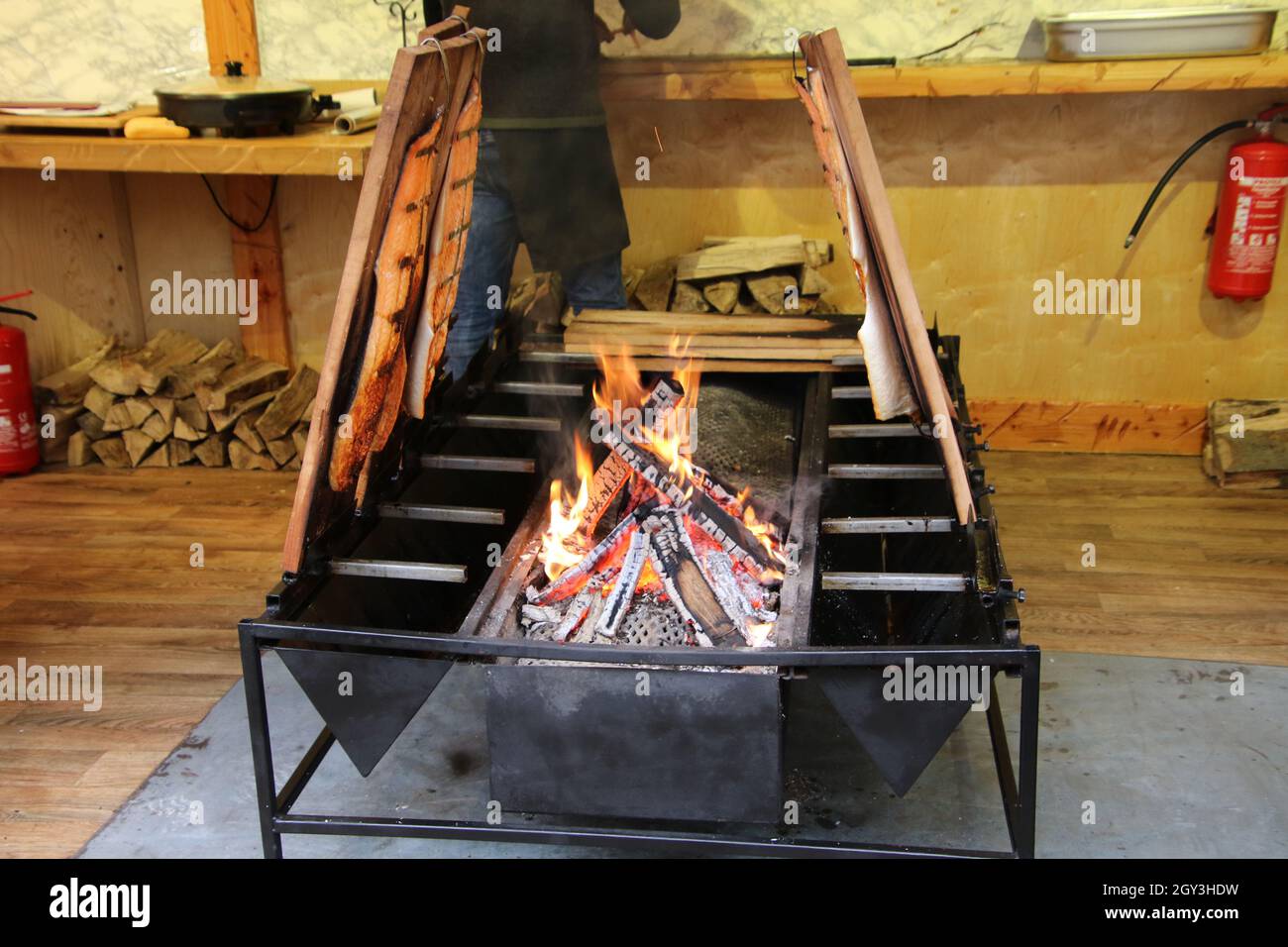 Salmon filets attached to wooden planks cooking over a wooden fire with ...