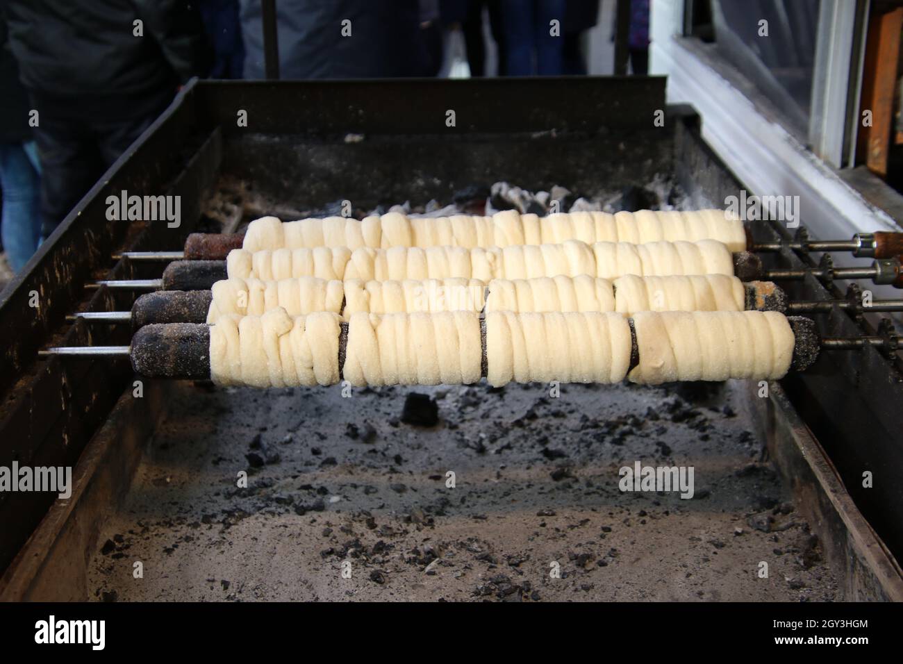 Four chimney cakes cooking on skewers over a metal coal covered plate ...