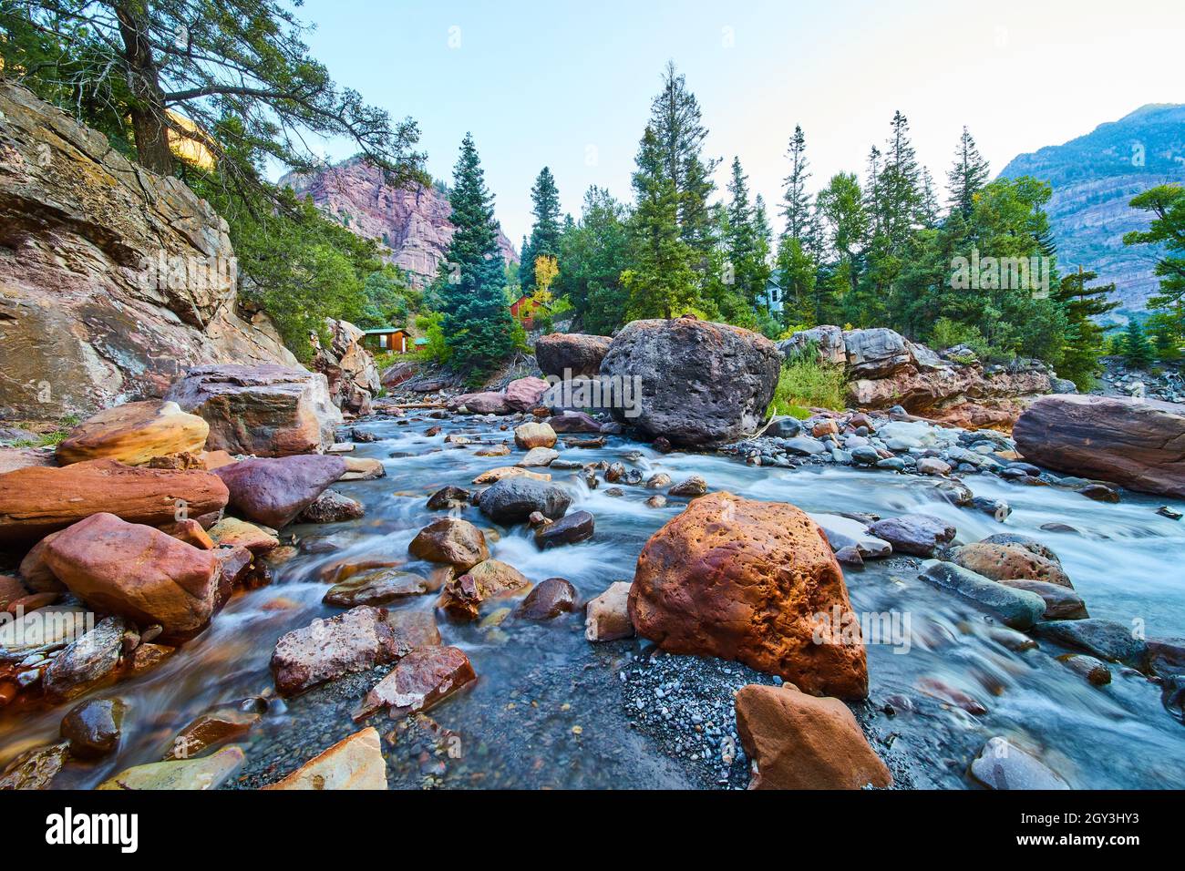 Red boulders in shallow riverbed against cliffs and mountains Stock ...