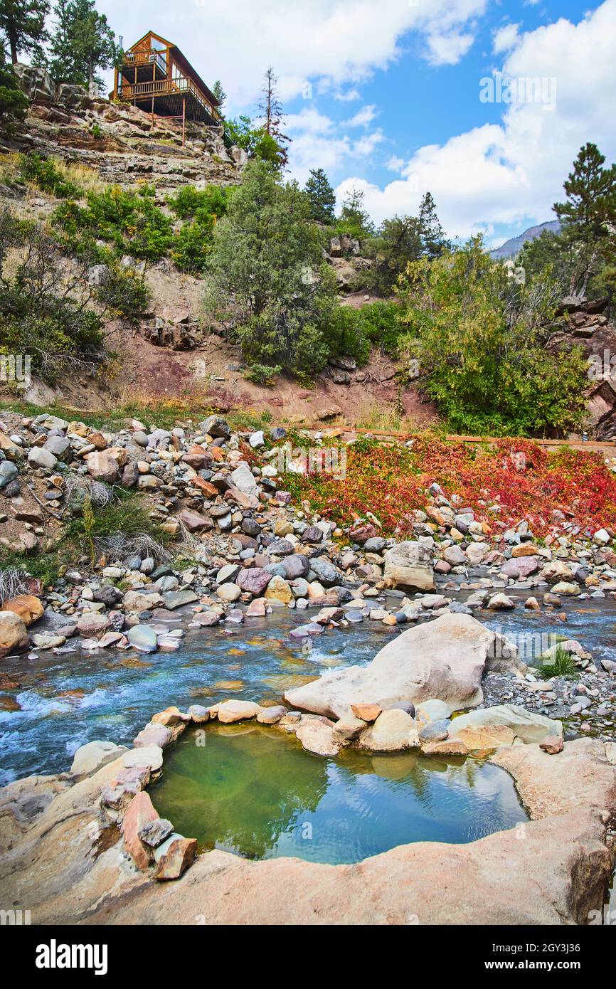 Natural small hot spring next to river and cliffs with log cabin at top ...