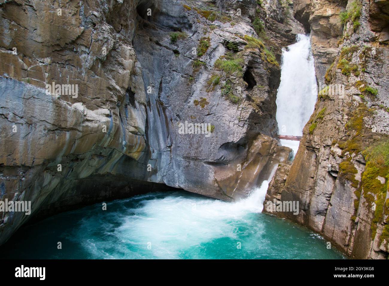 A waterfall going through a rock chasm into a clear green pool. The ...