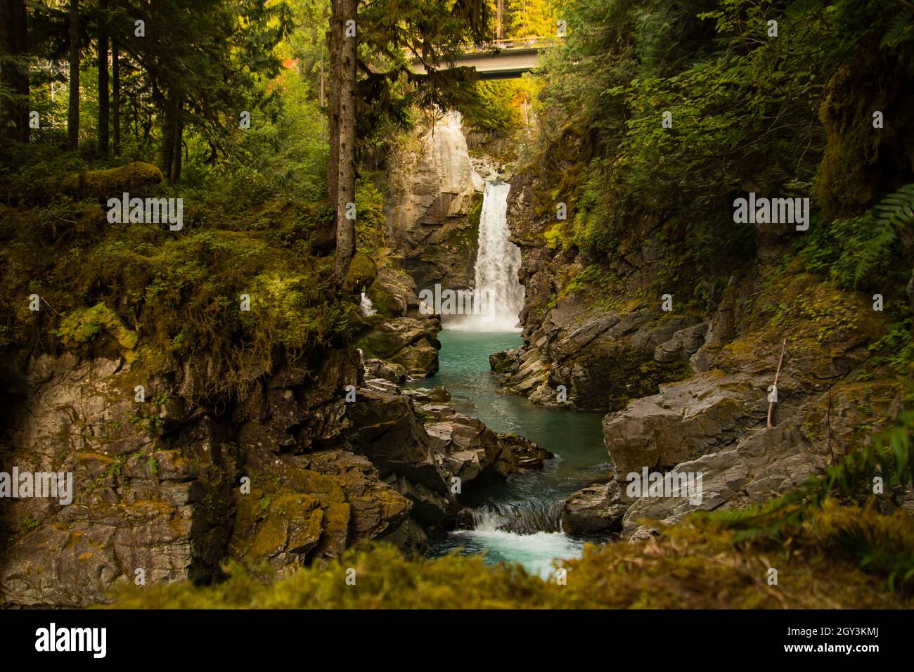 A waterfall under a bridge going over a rocky cliff into a clear blue ...