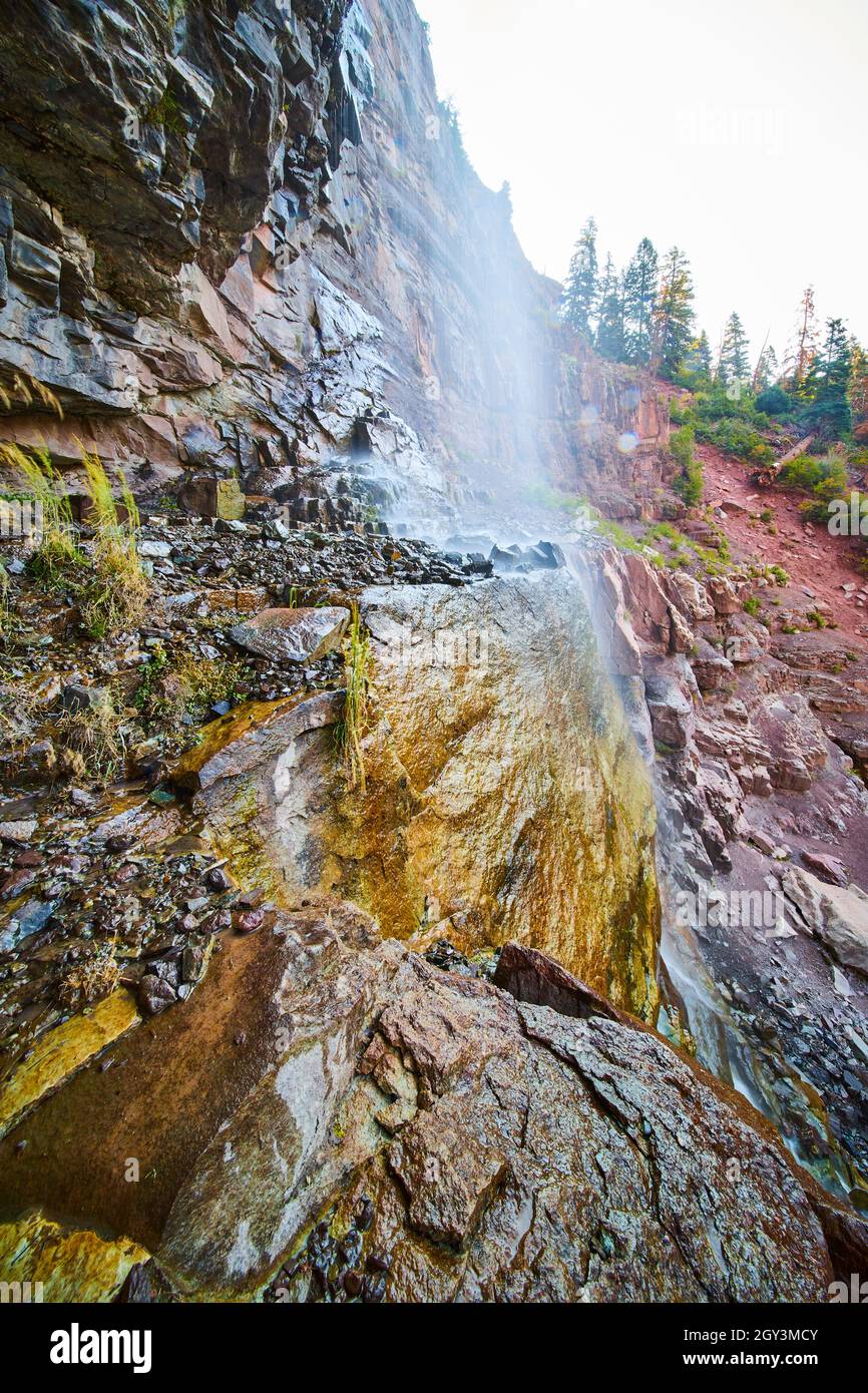 View from side of tall waterfall crashing down over colorful rock ...