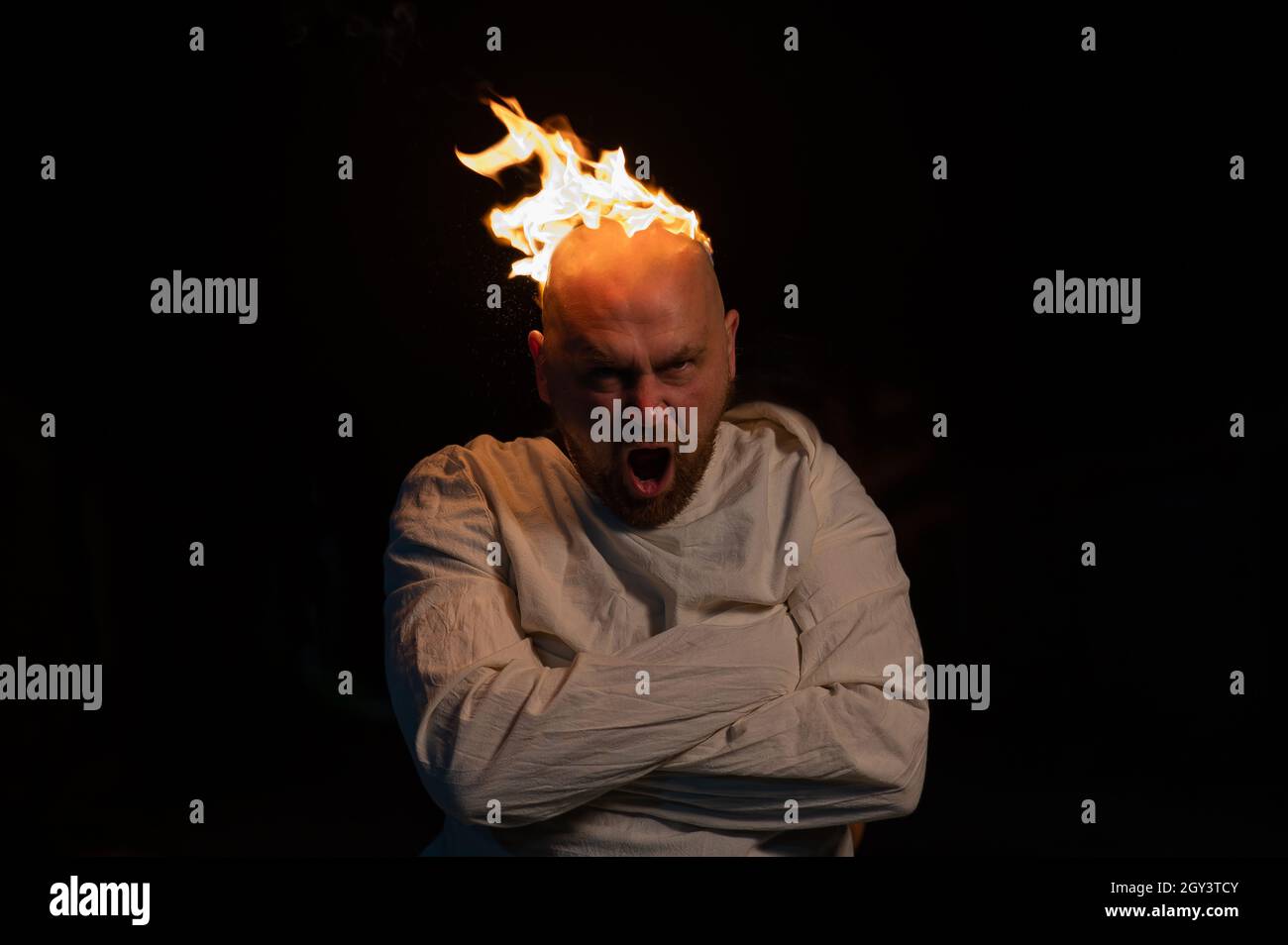 Bald man in a straitjacket with a burning head on a dark background ...