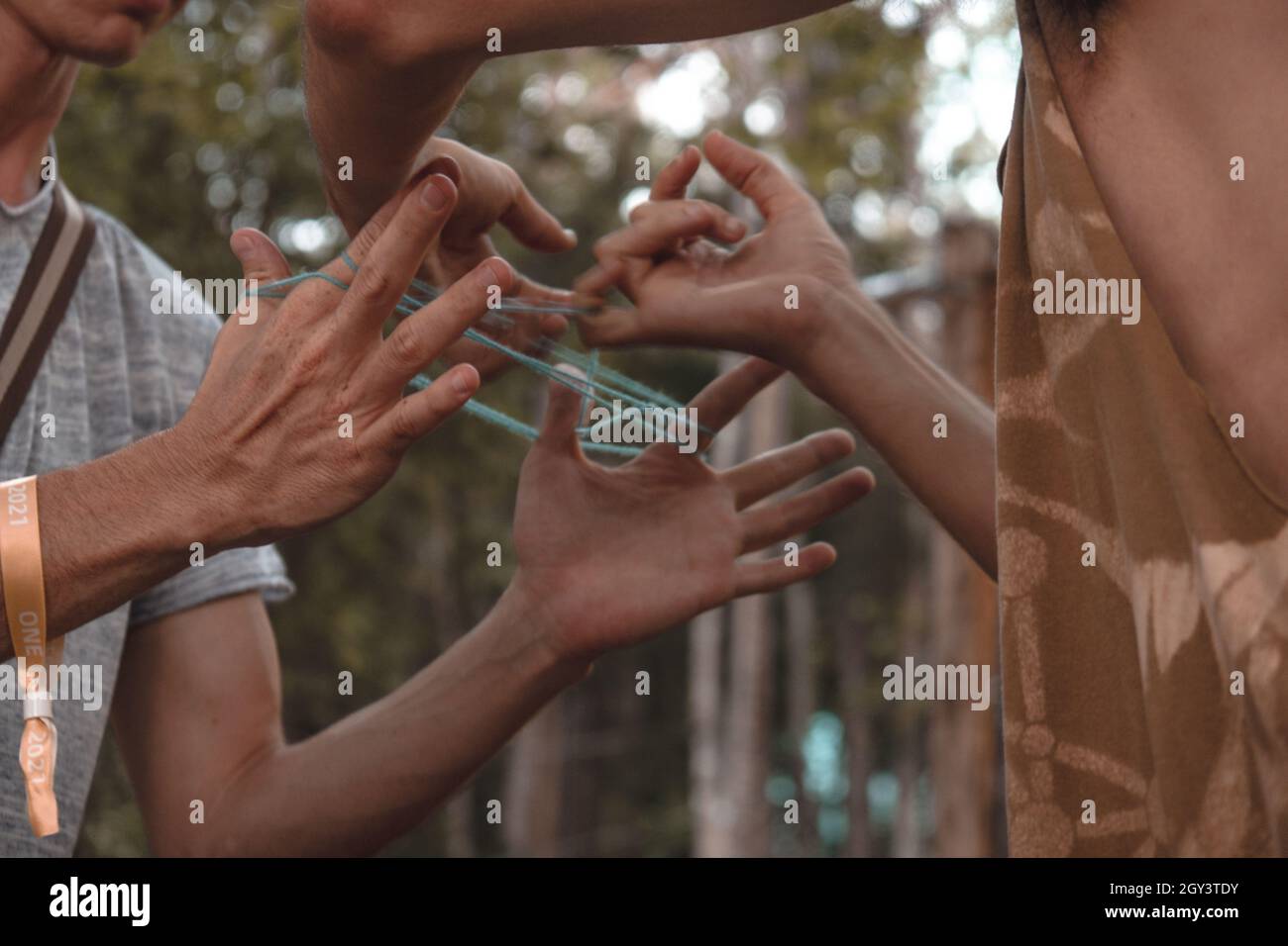 Closeup of two people playing the Cat's cradle with a thread outdoors ...