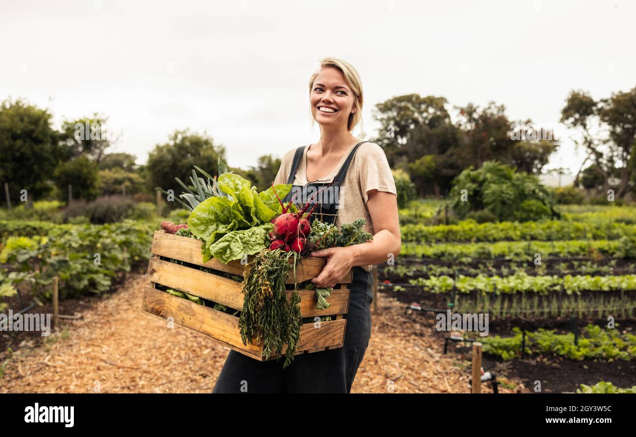 Happy female farmer holding a box with fresh produce. Young female ...