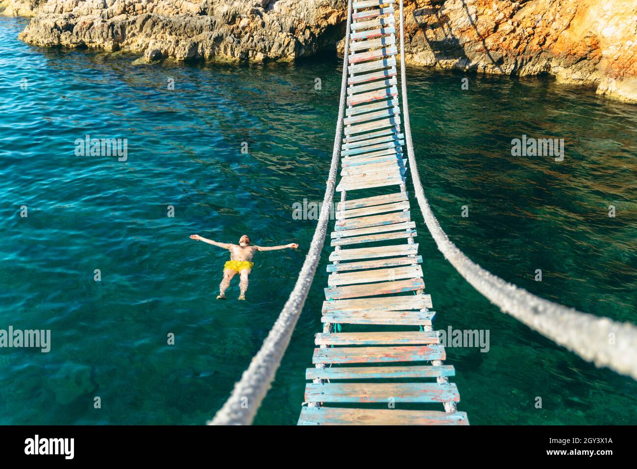 man floating in sea water on back. bay with rocky beach and suspension ...