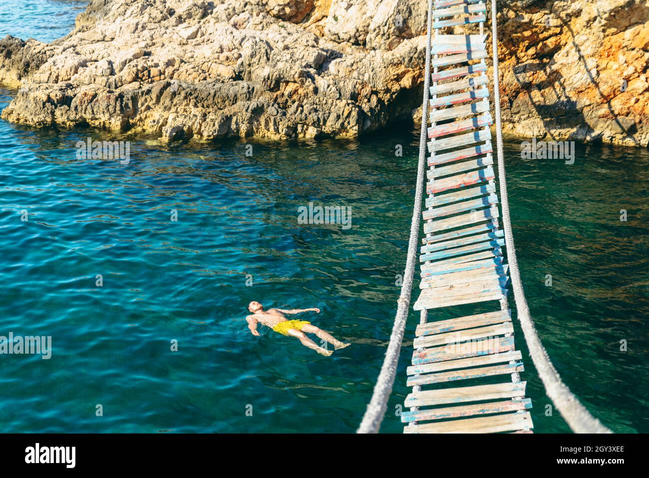 man floating in sea water on back. bay with rocky beach and suspension ...