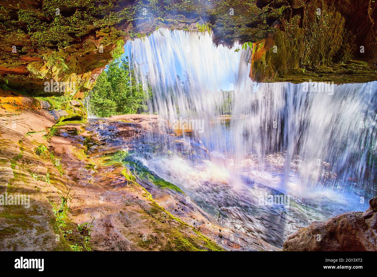 View behind and inside of waterfall cave of orange and lichen growth ...