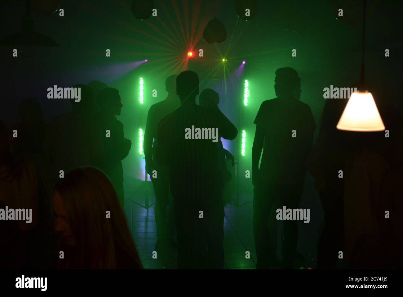 Silhouette of party goers dancing at a dance floor against green light ...