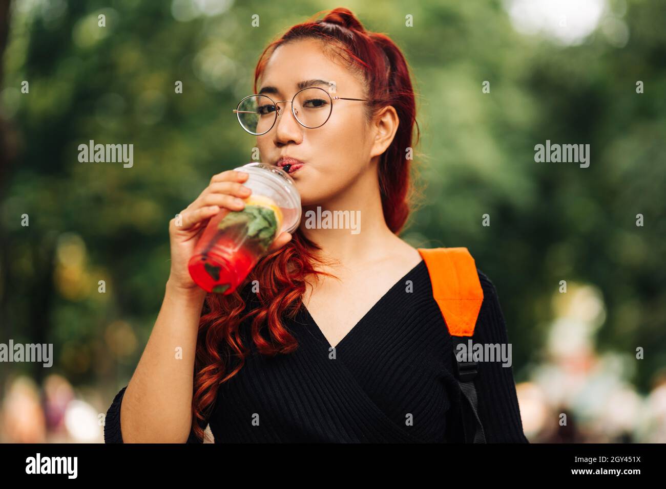 Portrait of smiling asian woman drinking cocktail while walking along ...