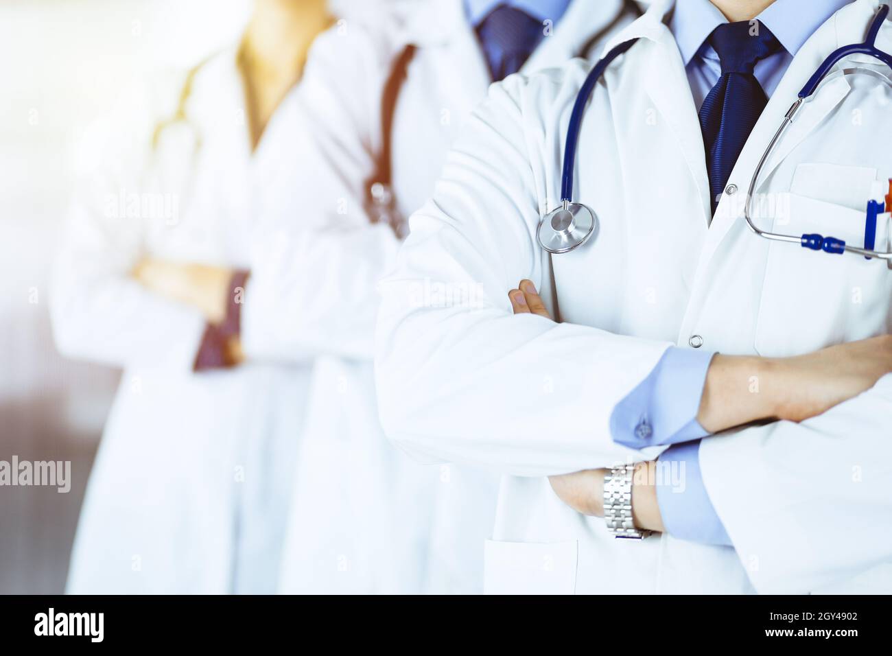 Group of modern doctors standing as a team with crossed arms and stethoscopes in a sunny ...