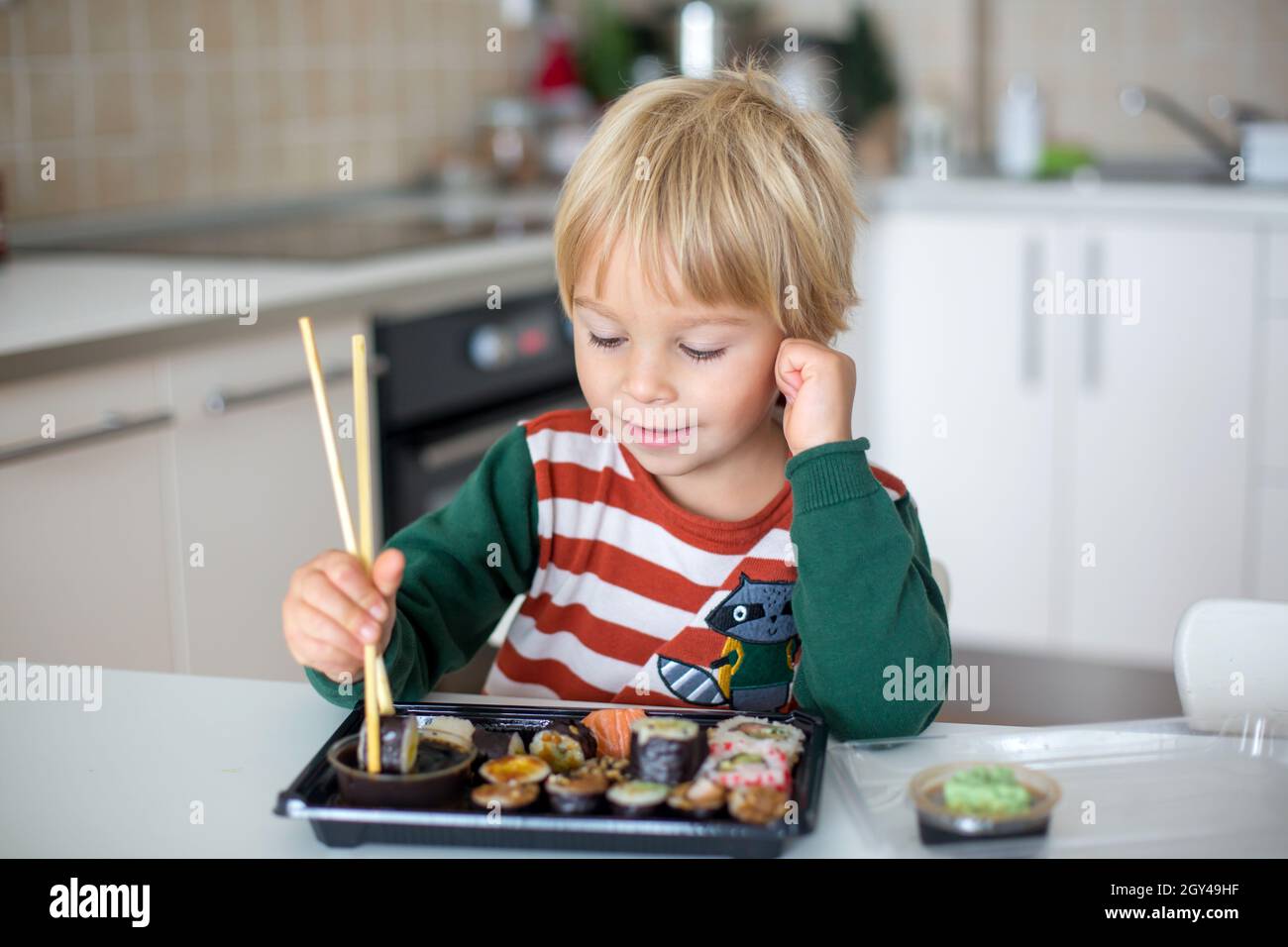 Cute blond child Eat Sushi Rolls At Home. Happy boy ready for eating ...