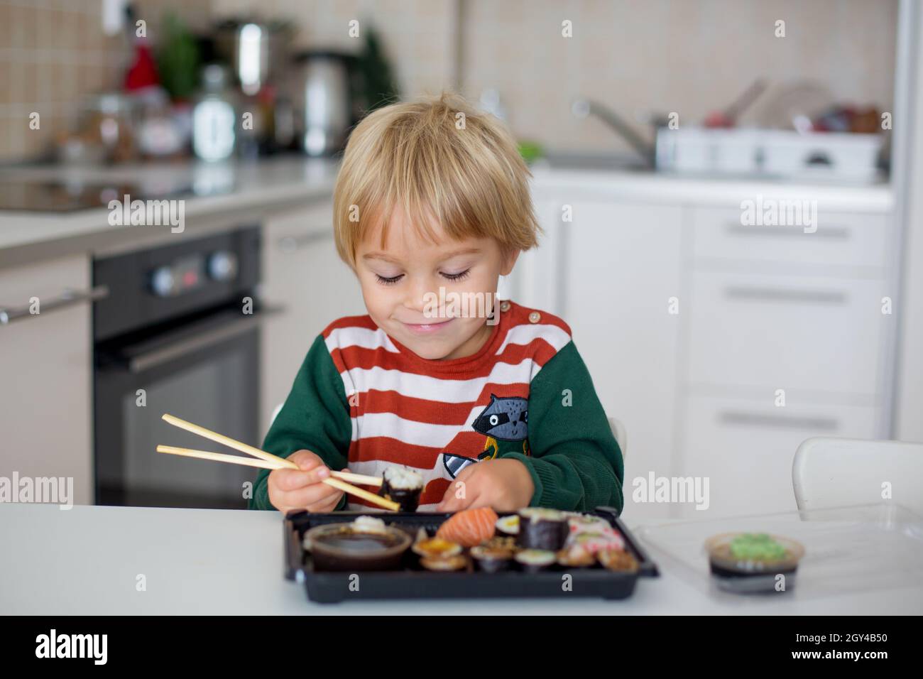 Cute blond child Eat Sushi Rolls At Home. Happy boy ready for eating ...