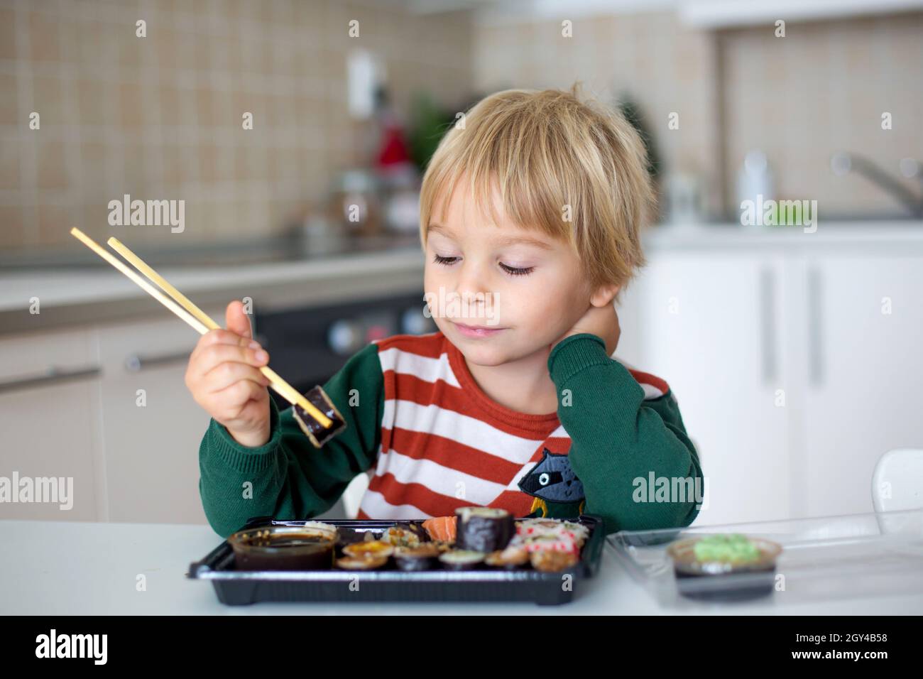 Cute blond child Eat Sushi Rolls At Home. Happy boy ready for eating ...