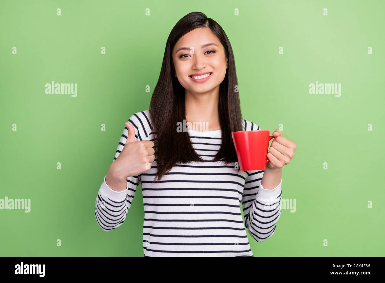 Portrait of attractive cheerful girl drinking beverage showing thumbup ...