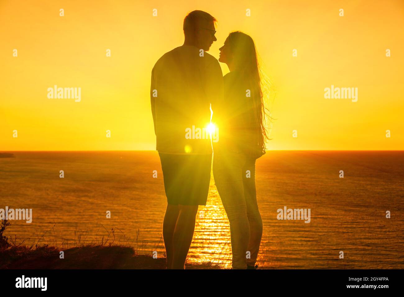 Silhouette of a young romantic couple enjoying an evening on a cliff ...