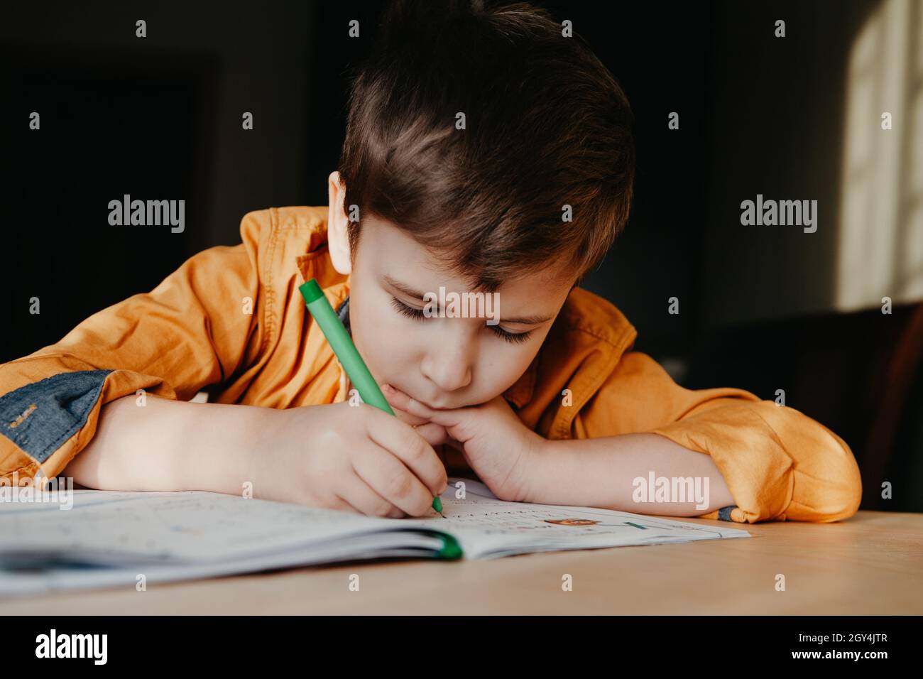 Cute 7 years old child doing his homework sitting by desk. Boy writing ...