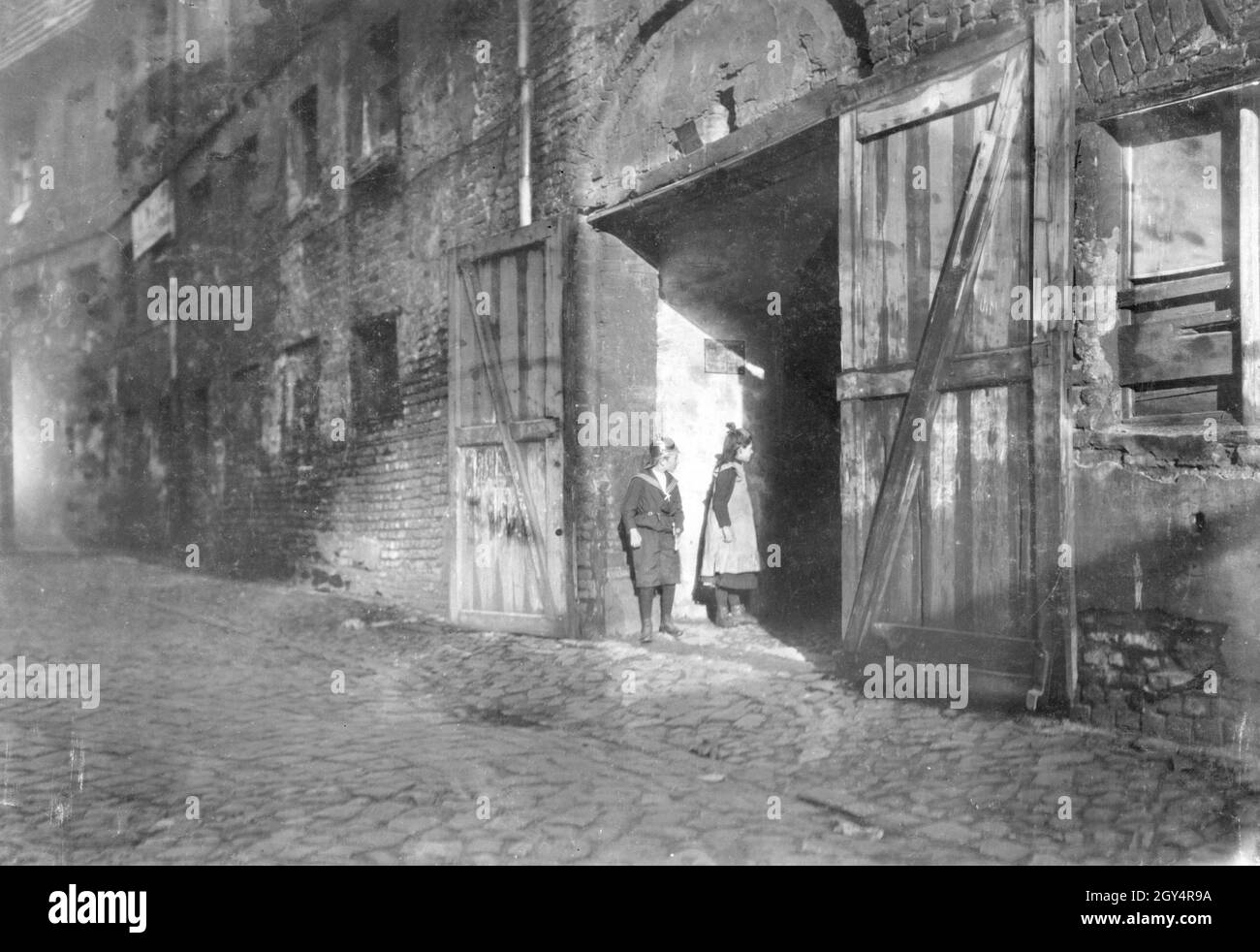 Two children are standing in a dilapidated courtyard entrance in the ...