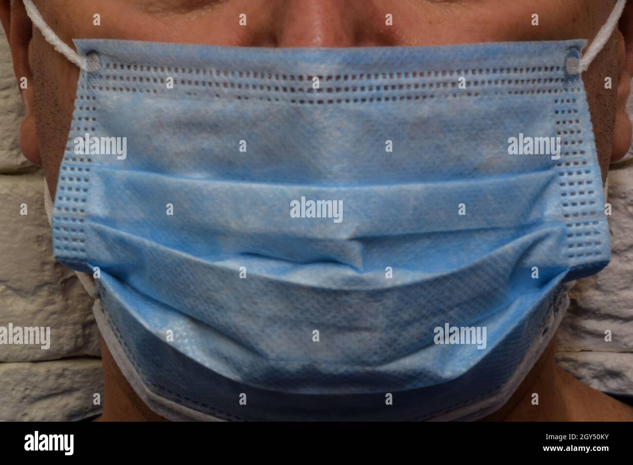 Blue medical mask on a male face close-up against a brick wall ...