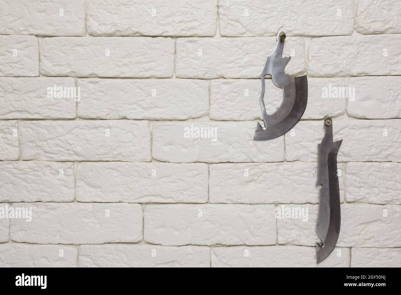 There are two kinds of knife blades hanging on the light brick wall on ...