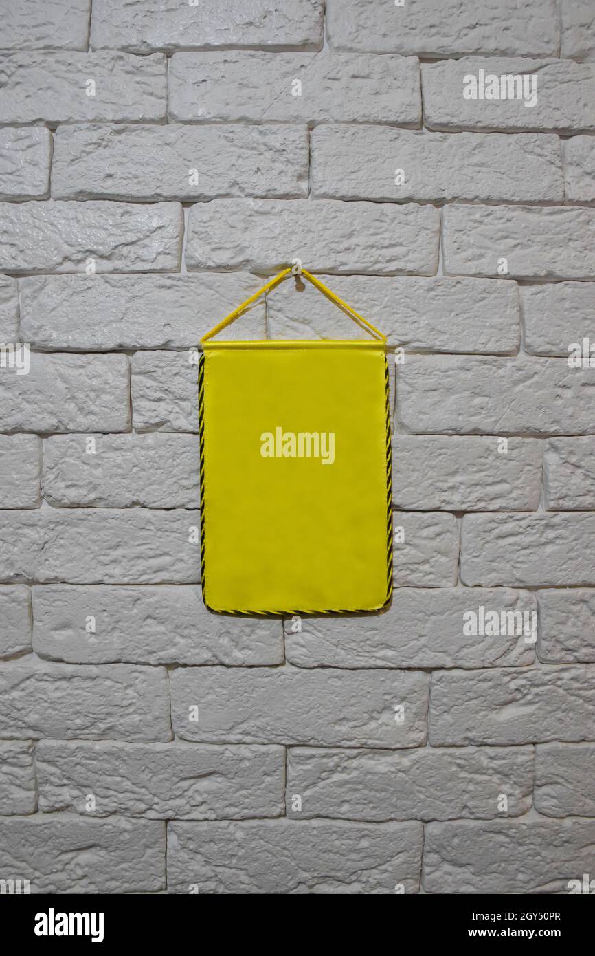 A yellow pennant hangs on a light-colored brick wall. The pennant is ...