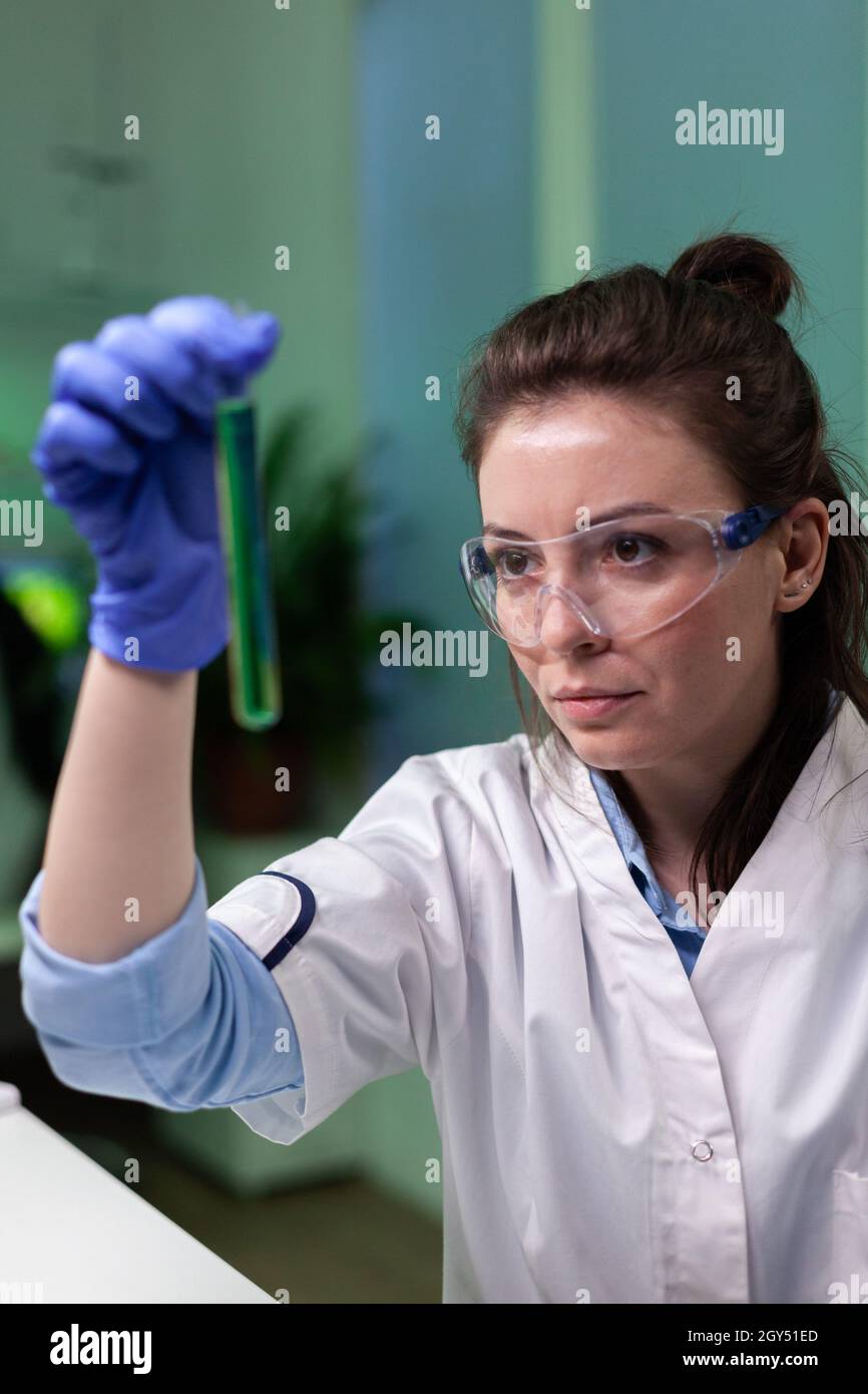 Portrait of biochemist doctor looking at medical test tube with green ...