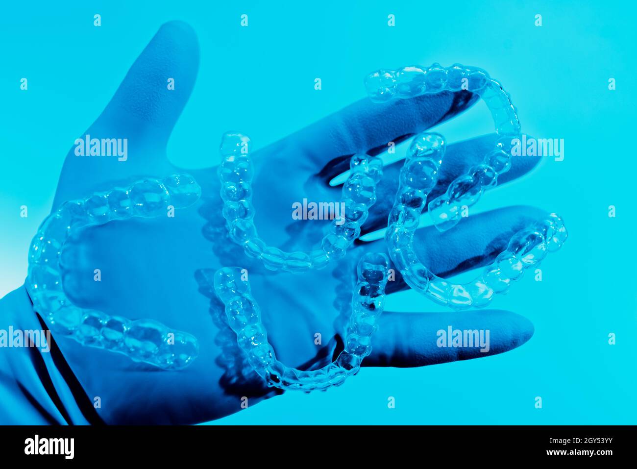 Invisible dental braces are held by a hand in a medical glove. Plastic ...