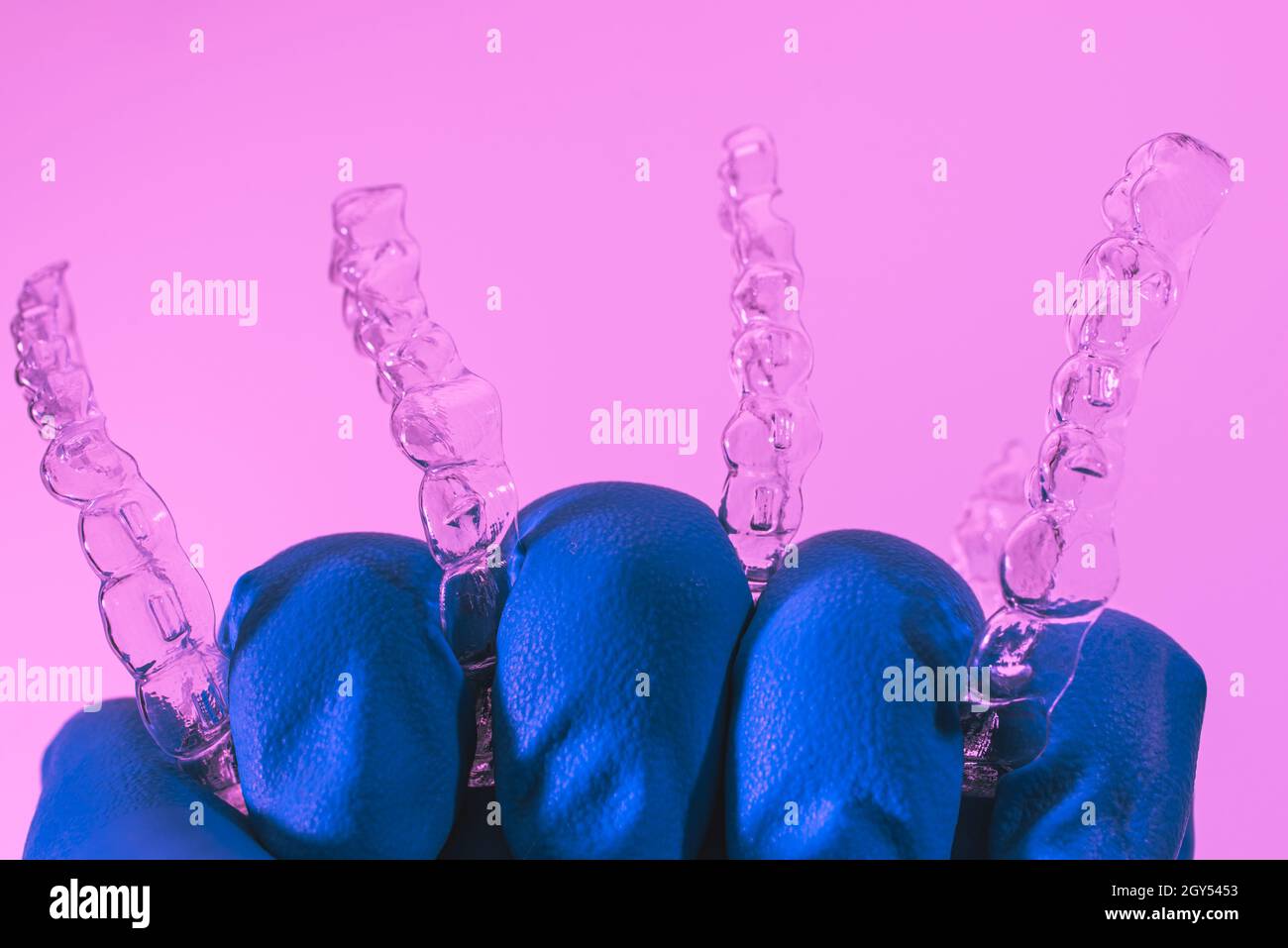 Invisible dental braces are held by a hand in a blue glove on a pink ...