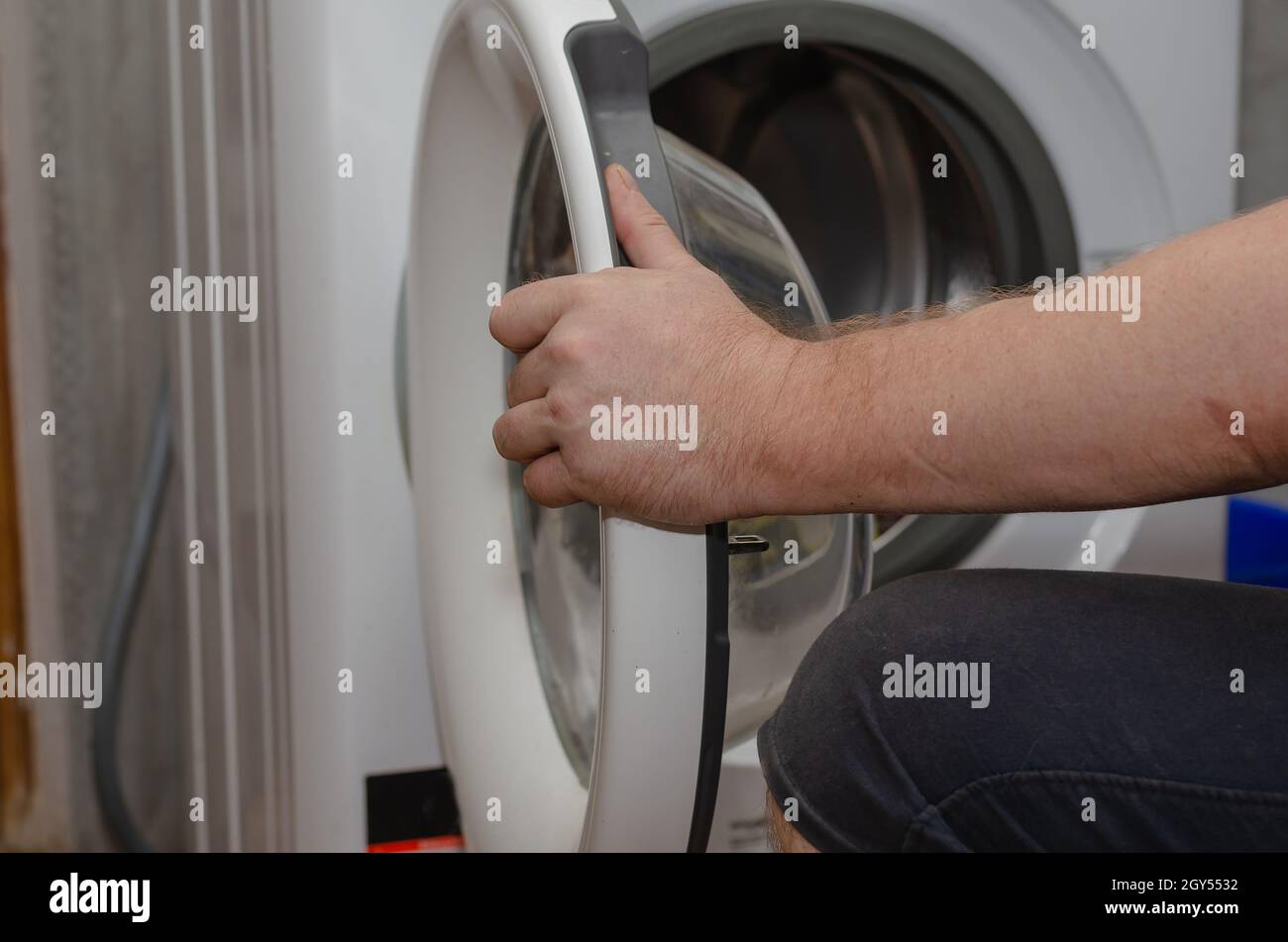 An adult man next to a washing machine. A hand closes the door of the ...