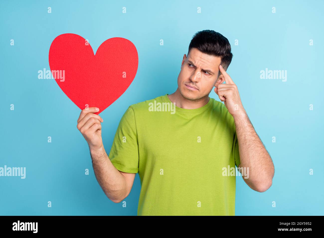 Photo of minded serious young man look heart shape red paper minded ...