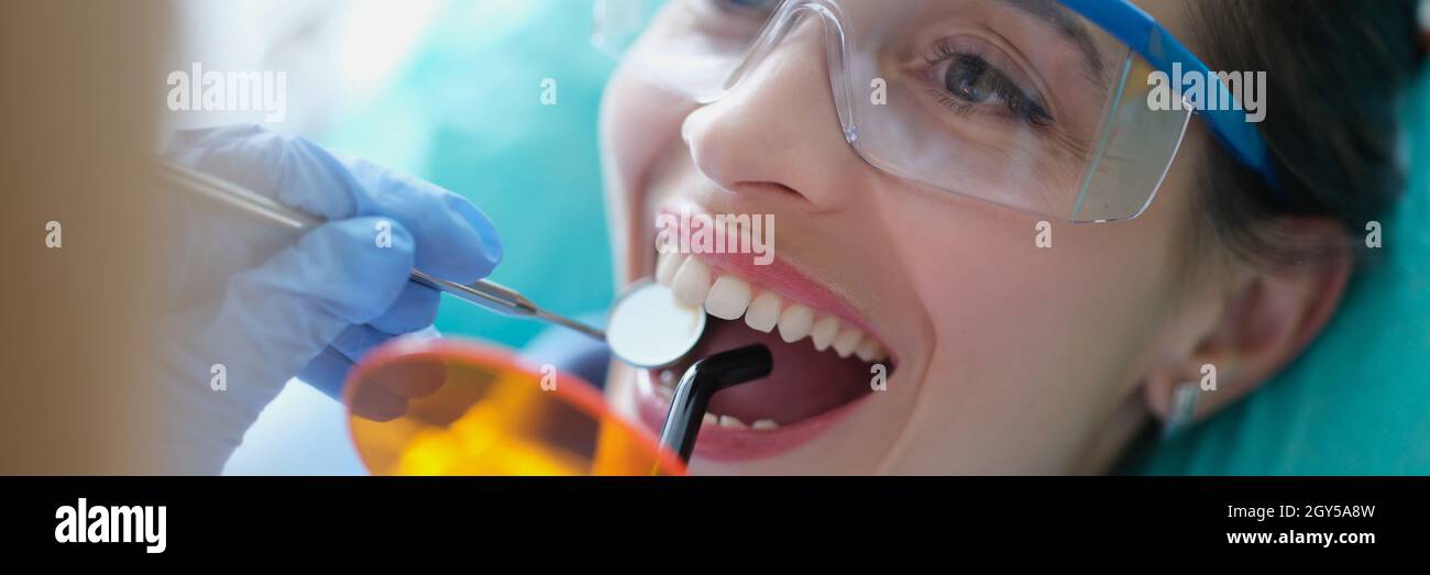 Dentist treating teeth to woman patient using curing light and dental ...