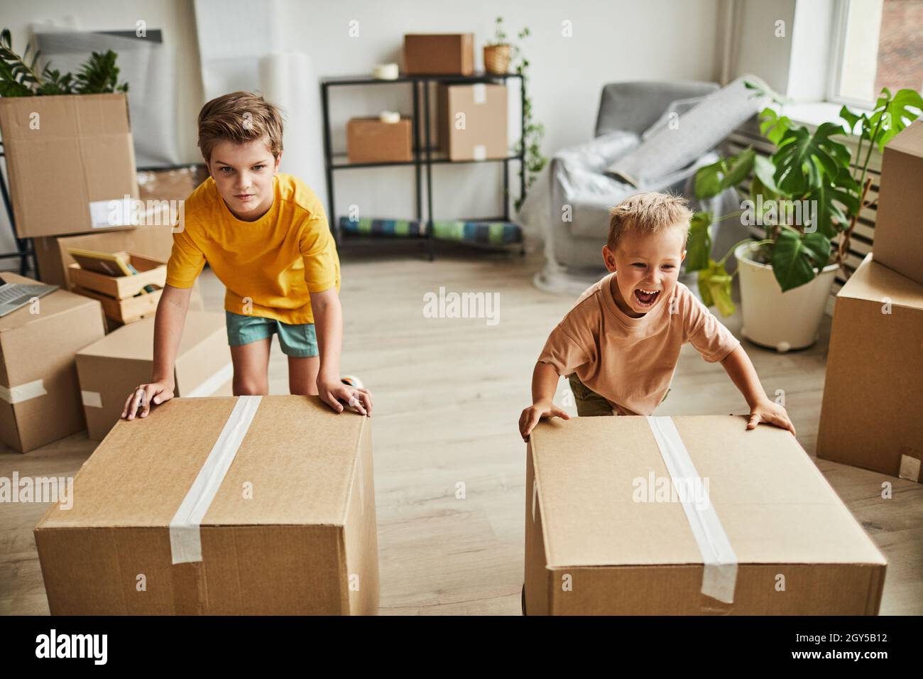 Portrait of two boys moving cardboard boxes while family relocating to ...
