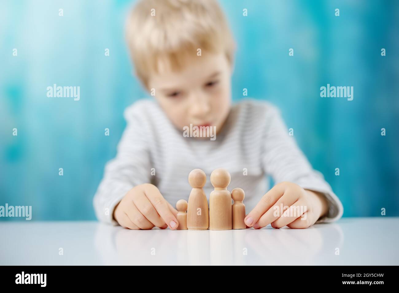 Child playing with wooden figures of the family on the blue background ...