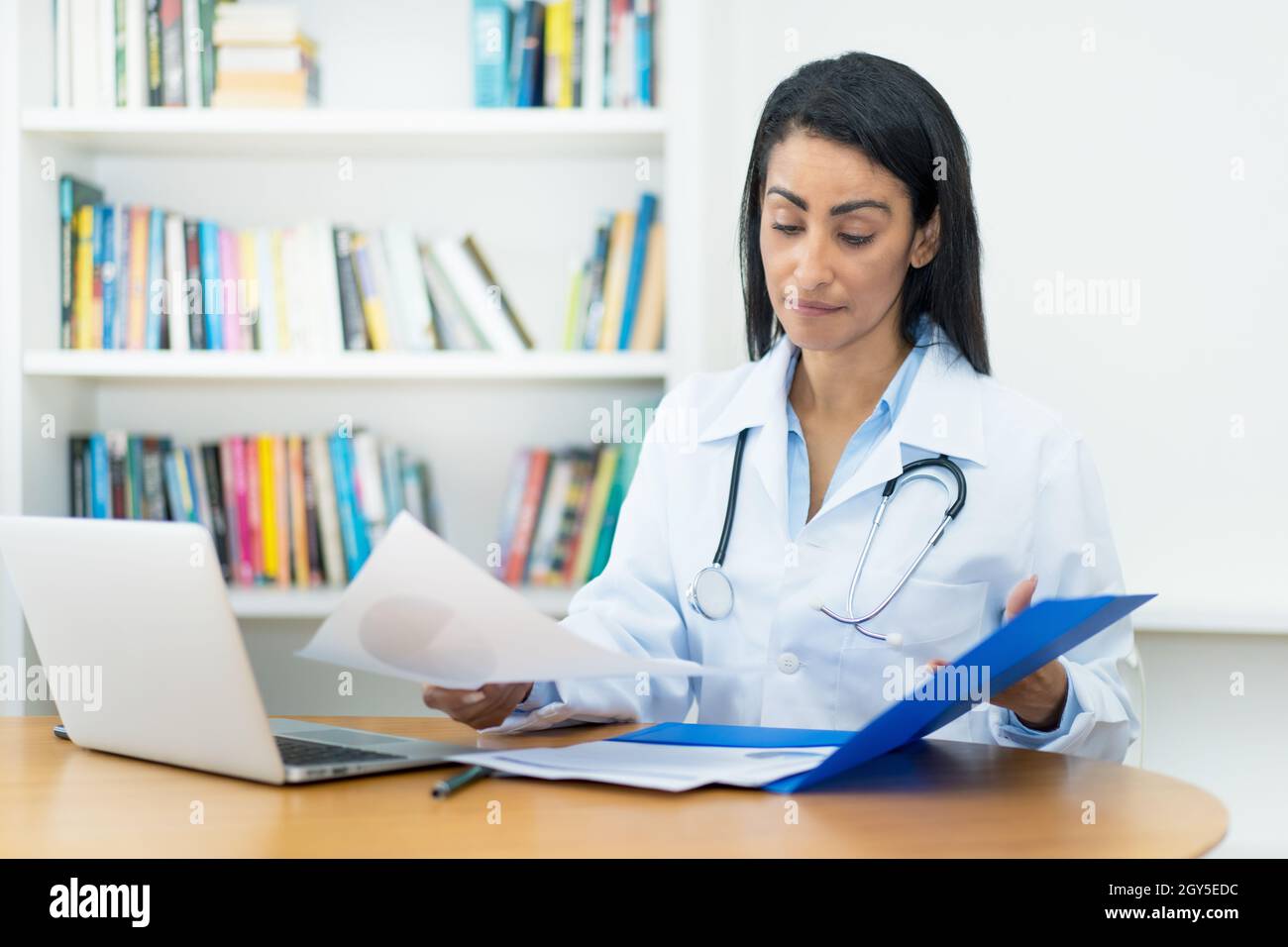 Serious latin american female gynecologist at desk at work at hospital ...