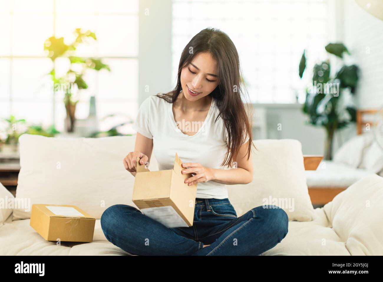 young woman sitting on the sofa and is happily unpacking her package ...
