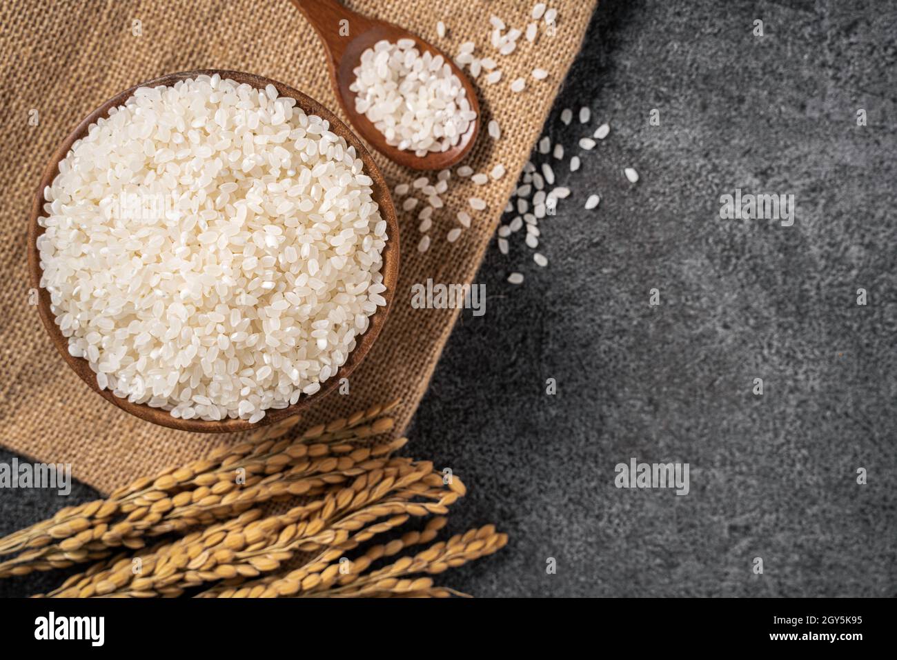 White raw rice in a bowl with the ear on the dark black table ...