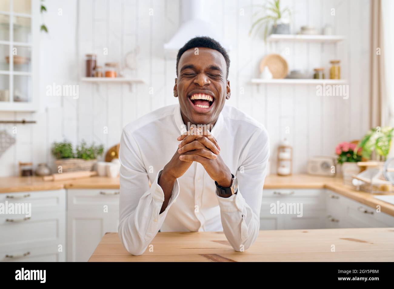 Laughing man sitting at the counter on the kitchen. Cheerful male ...
