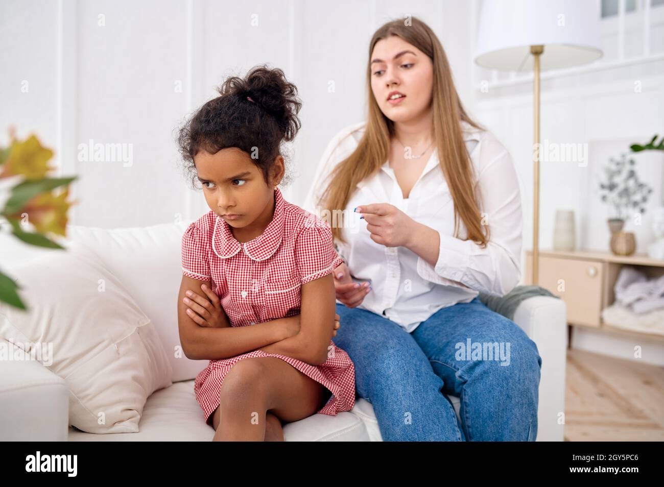 Mother scolds her little daughter on sofa in living room.Mom and sad ...