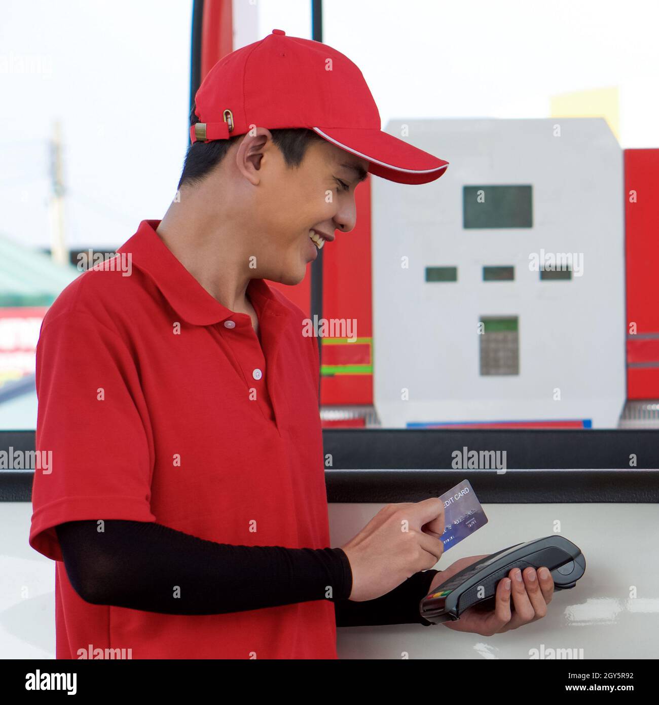 Gas station worker in red uniform stand smiling, swipe mockup credit ...