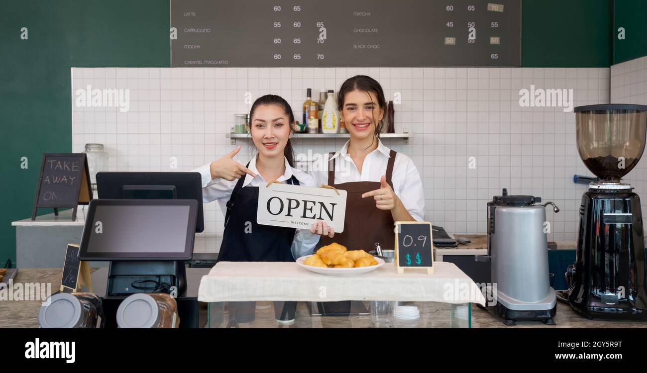 Young asian shopkeeper and caucasian barista with a smile holds an OPEN ...