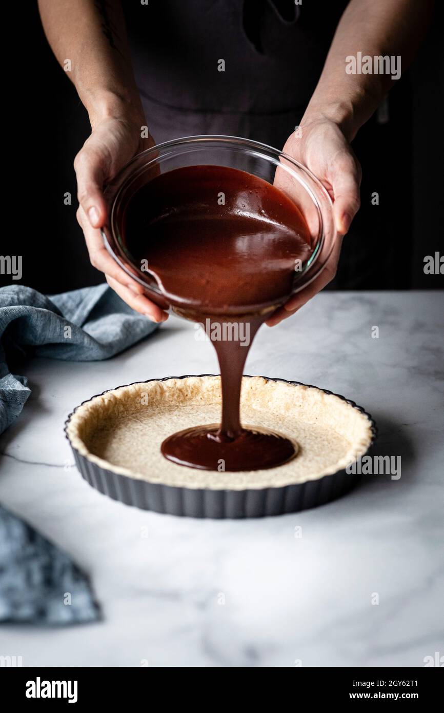 A baker pouring melted chocolate ganache into a tart shell Stock Photo ...