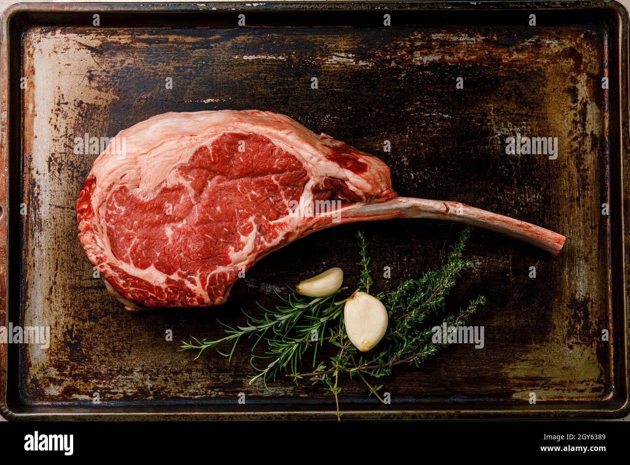 Raw fresh meat Tomahawk Steak and seasonings on dark baking sheet ...