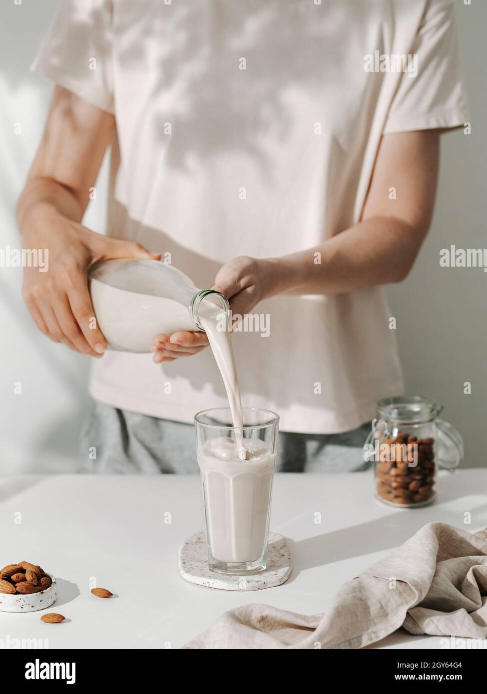 Unrecognizable woman pouring almond vegan milk into glass. Vertical ...