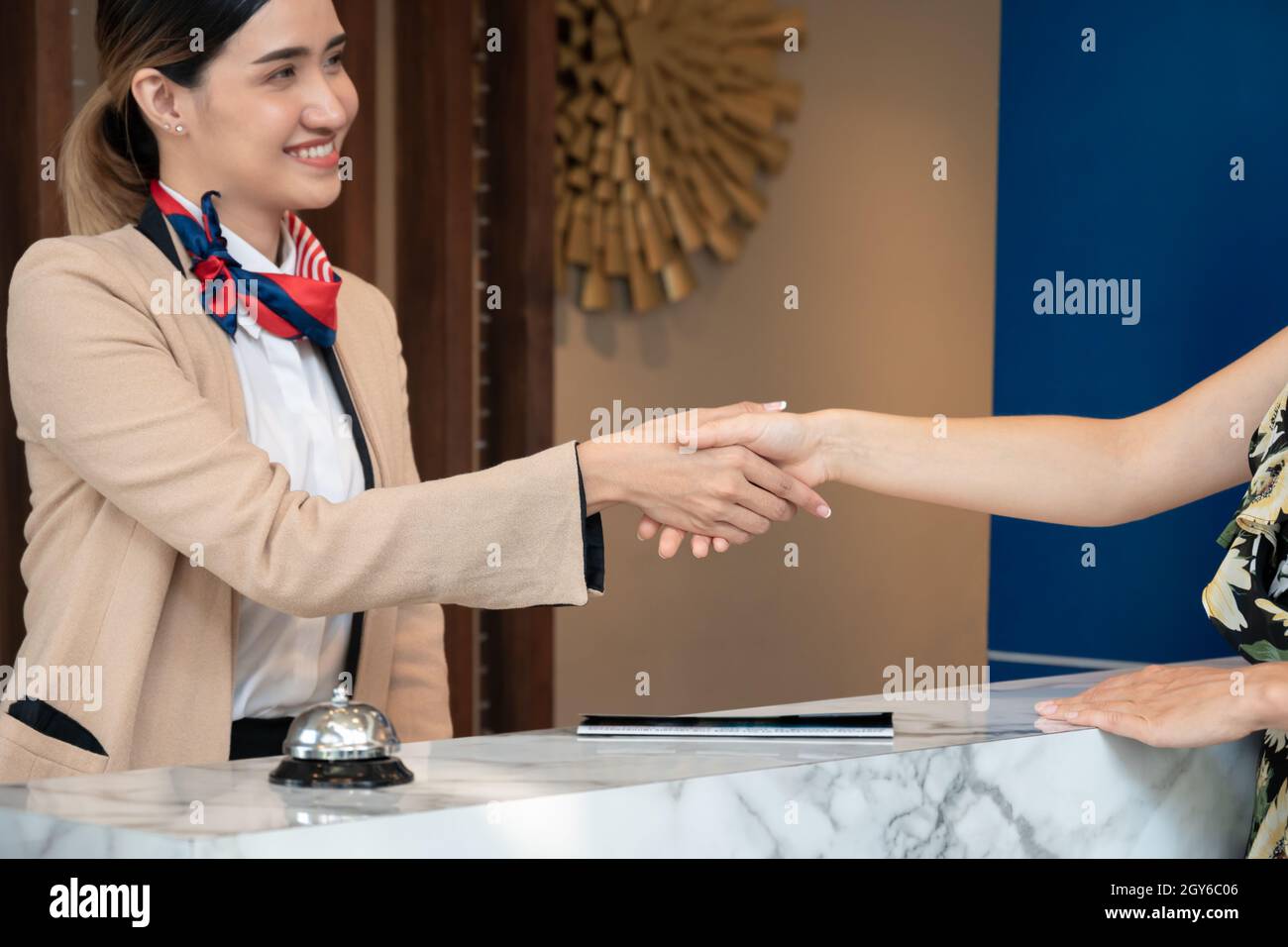 Smiling receptionist in hotel giving handshake to female guest across ...